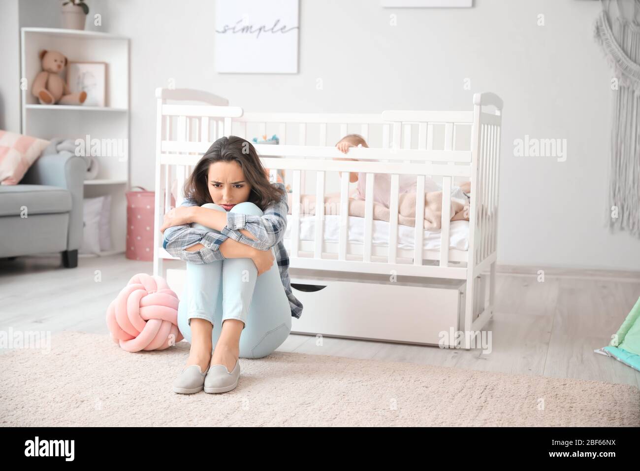 Young woman suffering from postnatal depression near bed with baby at ...