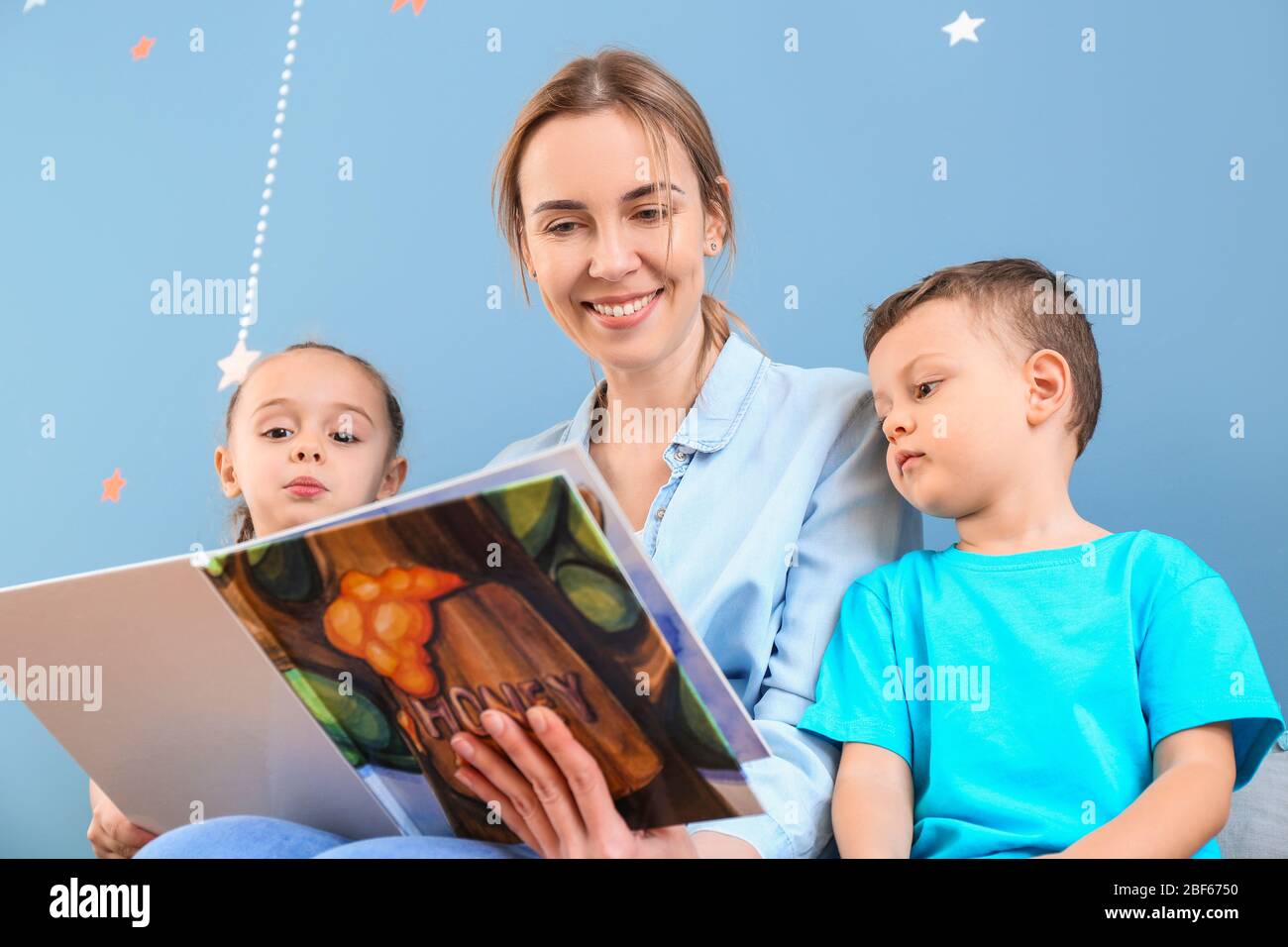 Nanny and cute little children reading book at home Stock Photo - Alamy