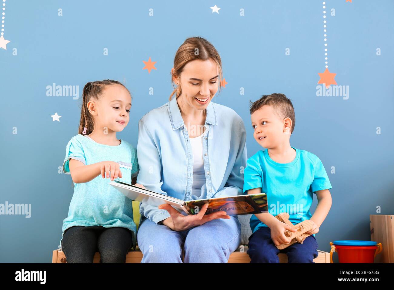 Nanny and cute little children reading book at home Stock Photo - Alamy