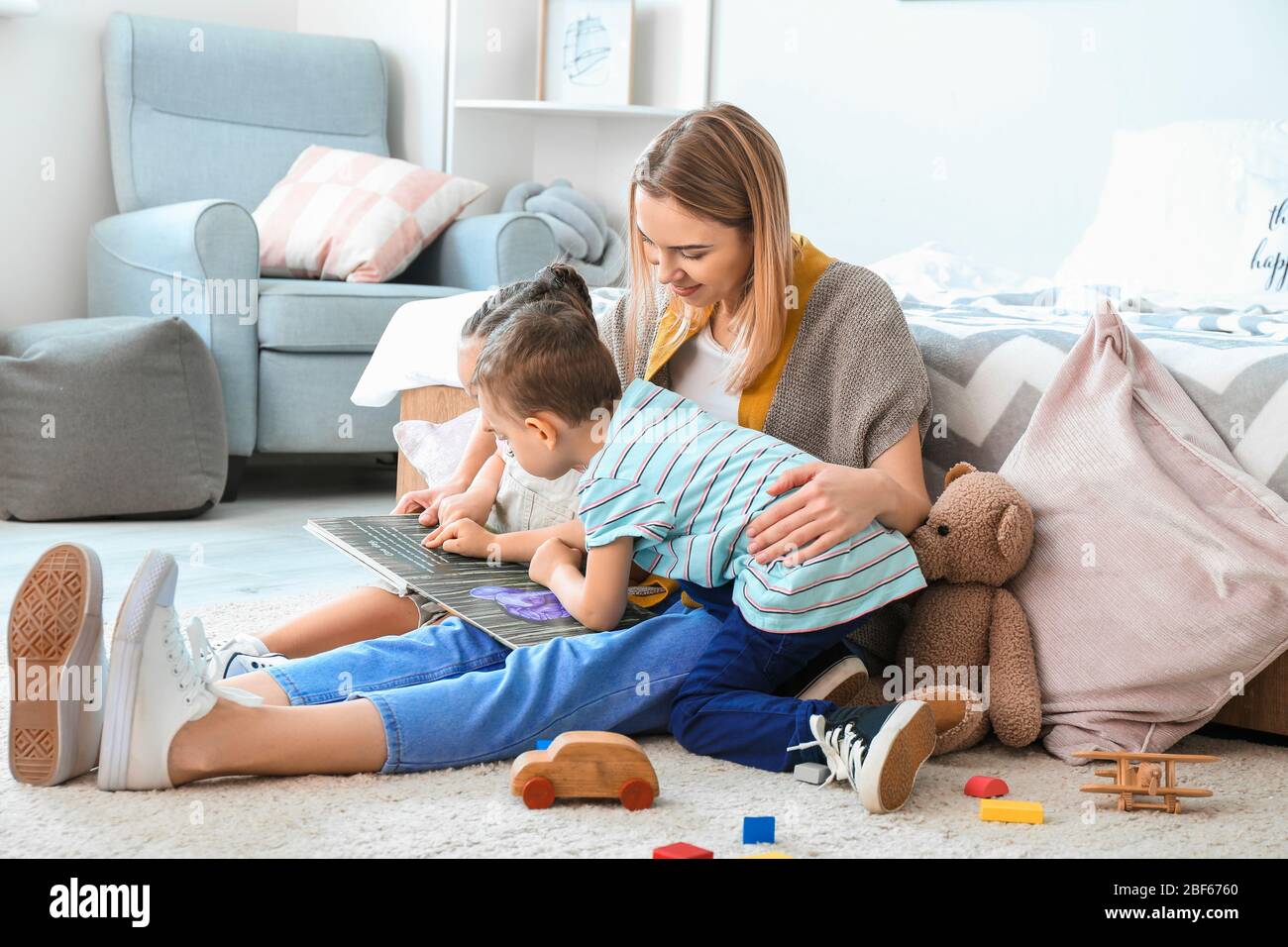 Nanny and cute little children reading book at home Stock Photo - Alamy