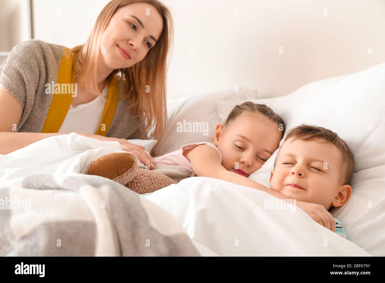 Nanny putting cute little children to bed Stock Photo - Alamy