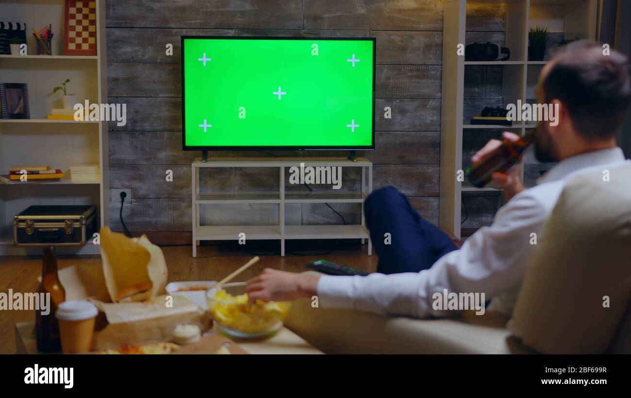 Back view of young entrepreneur relaxing watching tv. Green screen and ...
