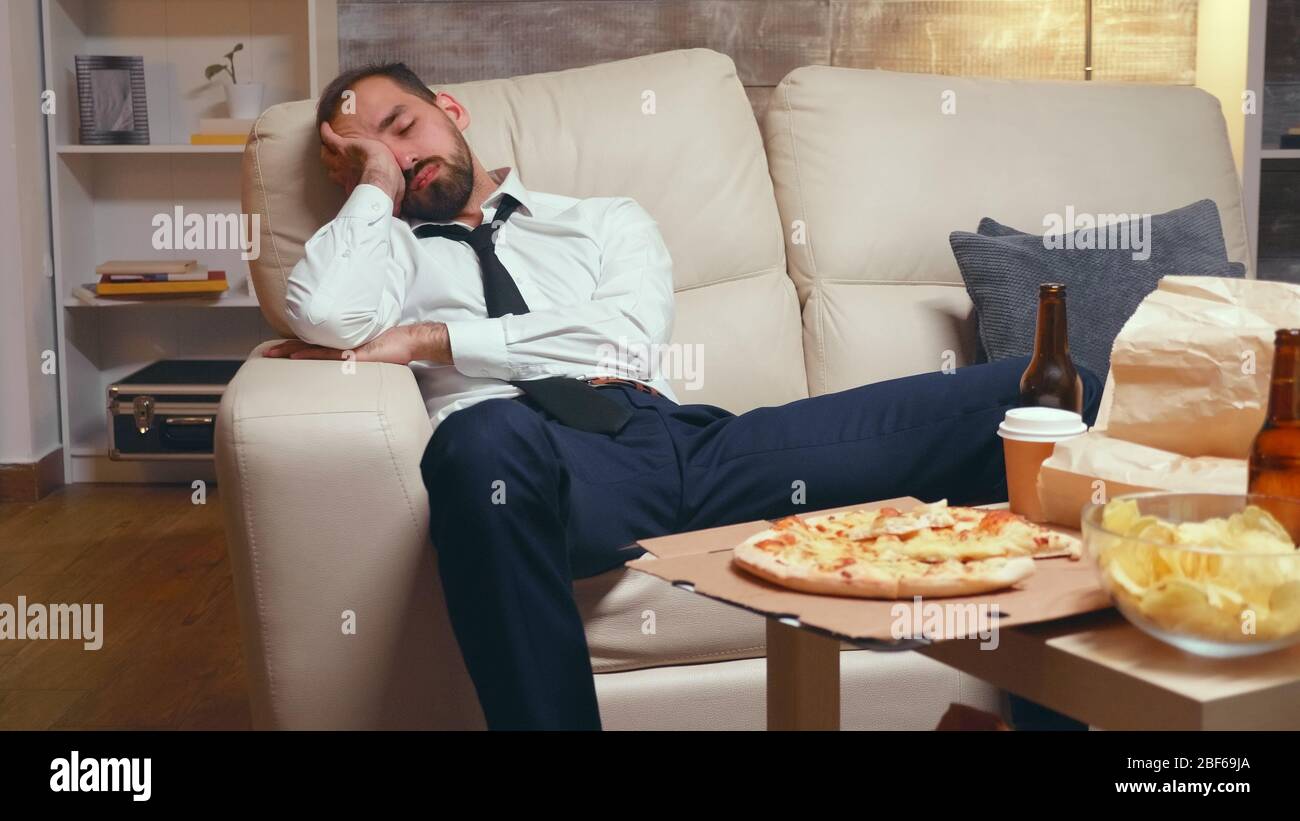 Overworked businessman sleeping on the couch. Fast food on the table ...