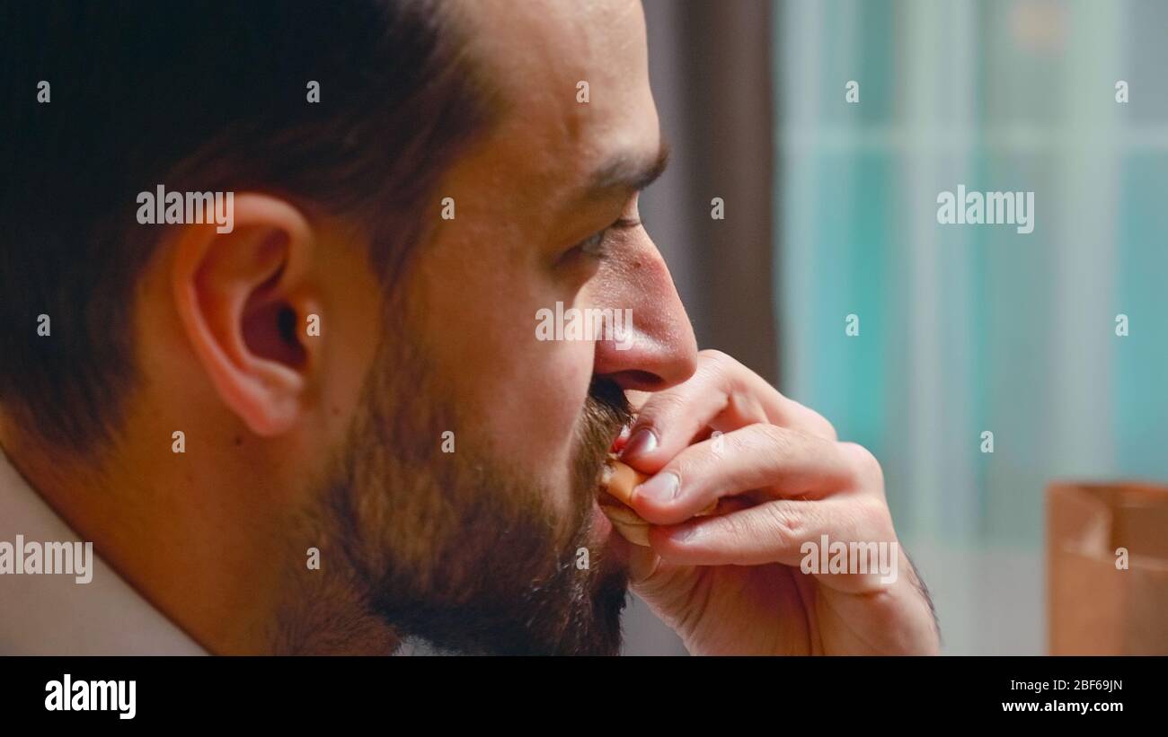Close up of businessman biting from a burger in living room. Tasty fast ...