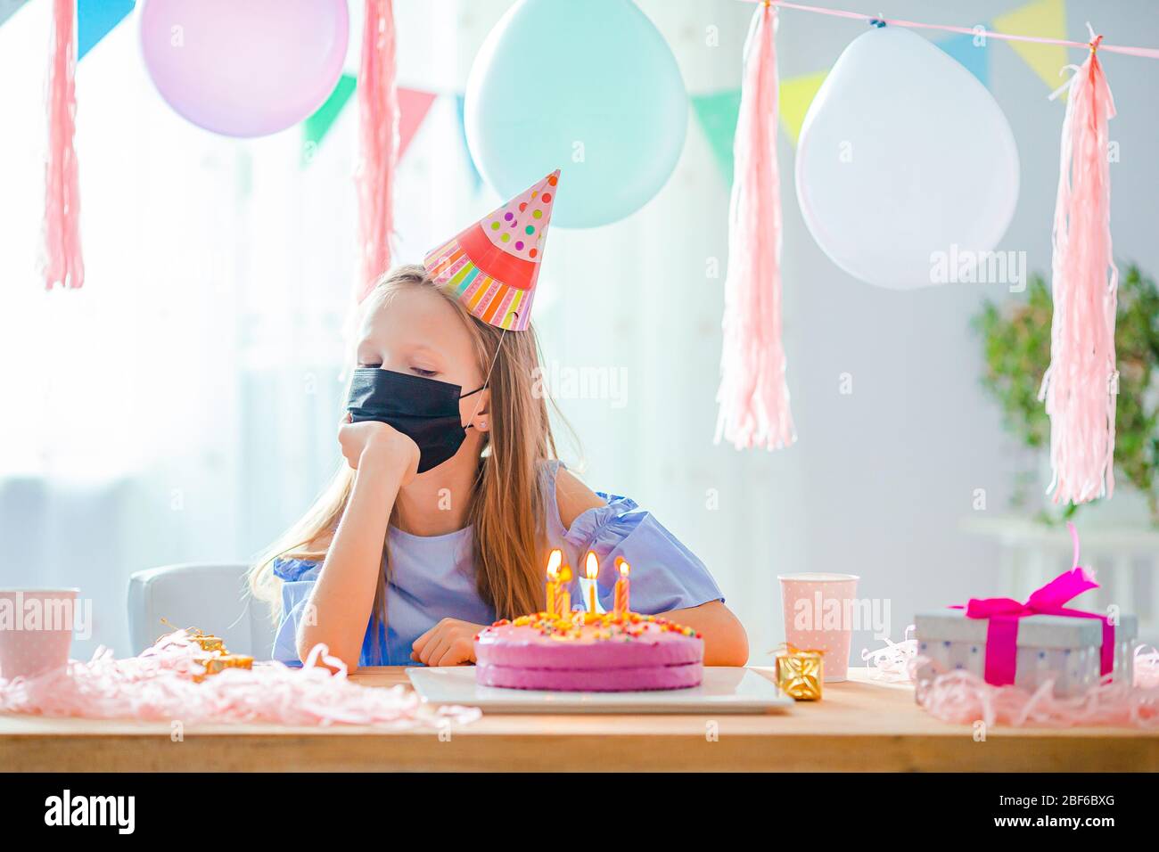 Caucasian girl is dreamily smiling and looking at birthday rainbow cake ...