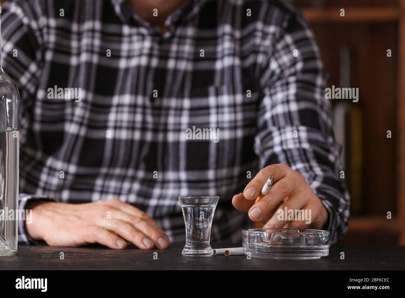 Man with glass of vodka smoking cigarette in bar. Concept of alcoholism ...