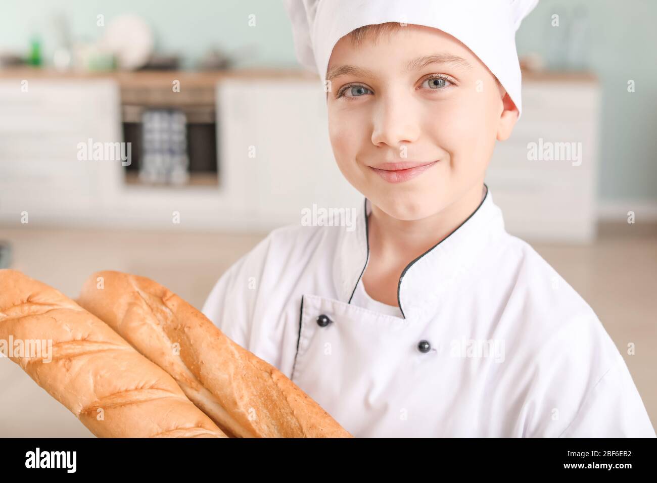Cute little chef with bread in kitchen Stock Photo - Alamy
