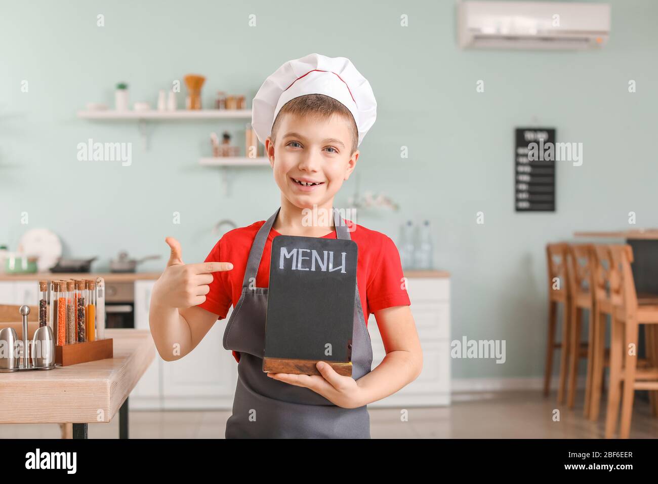 Cute little chef with menu in kitchen Stock Photo - Alamy