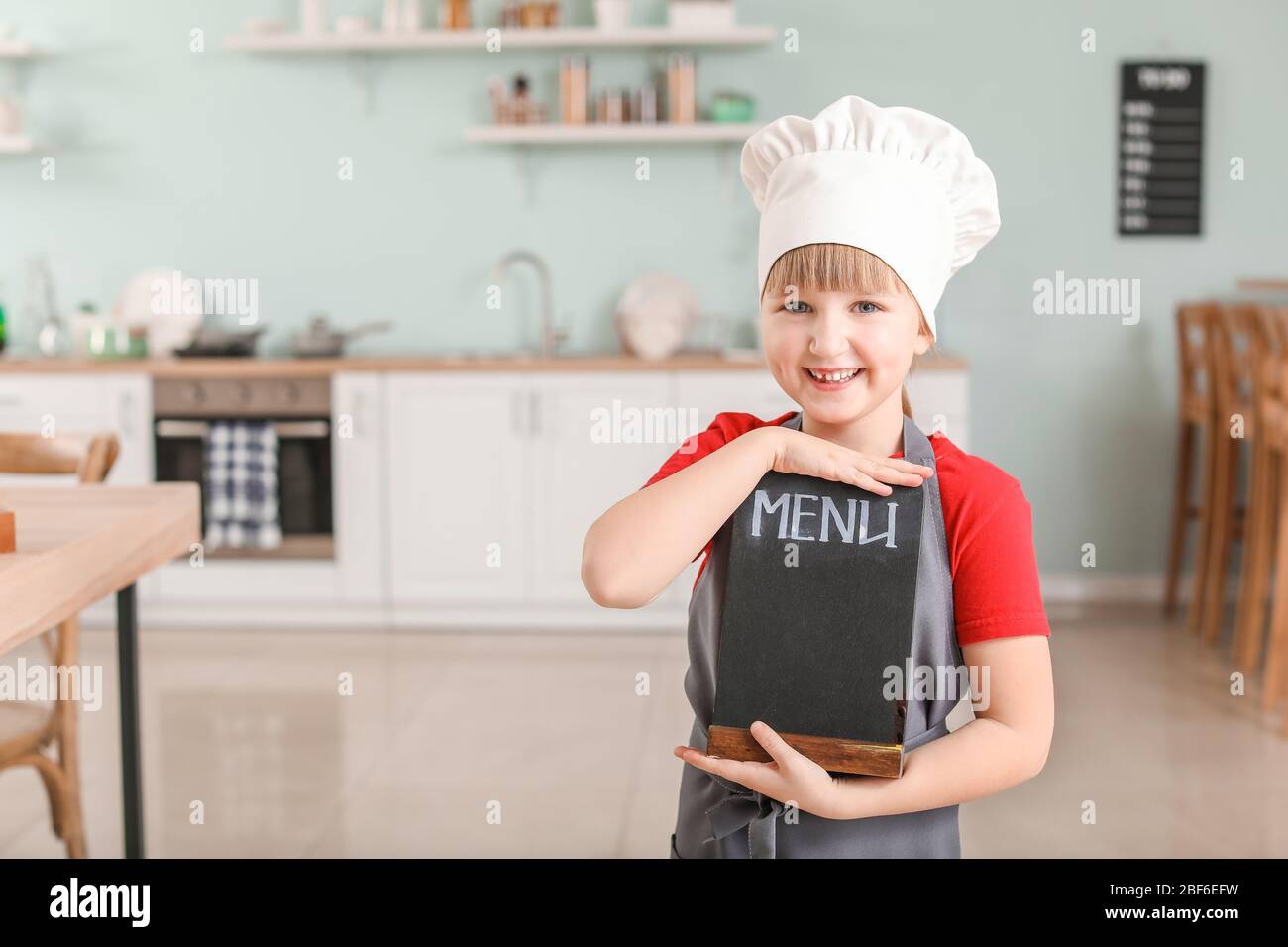 Cute little chef with menu in kitchen Stock Photo - Alamy