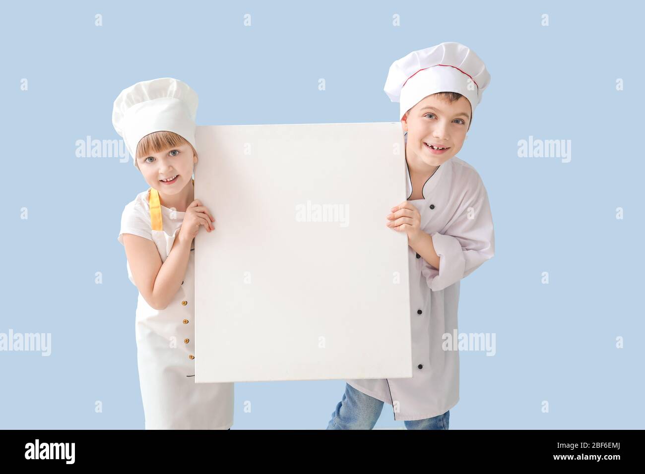 Cute little chefs with blank poster on color background Stock Photo - Alamy