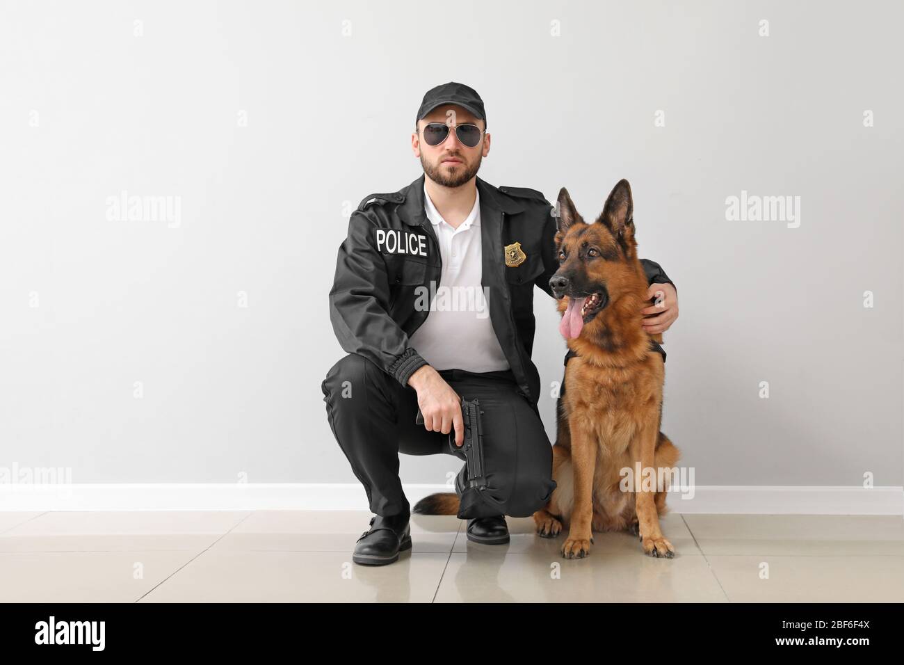 Male police officer with dog near light wall Stock Photo - Alamy