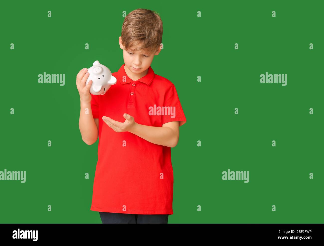 Cute boy tipping money from piggy bank on color background Stock Photo ...