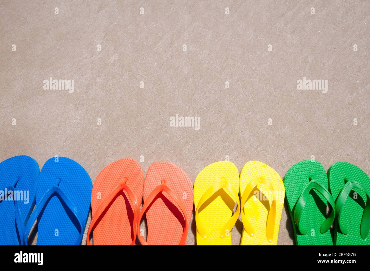Group of flip-flops in bright summer colors lined up on smooth sand ...