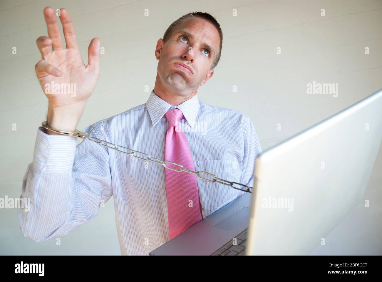 Exasperated businessman handcuffed to his laptop computer struggling to ...
