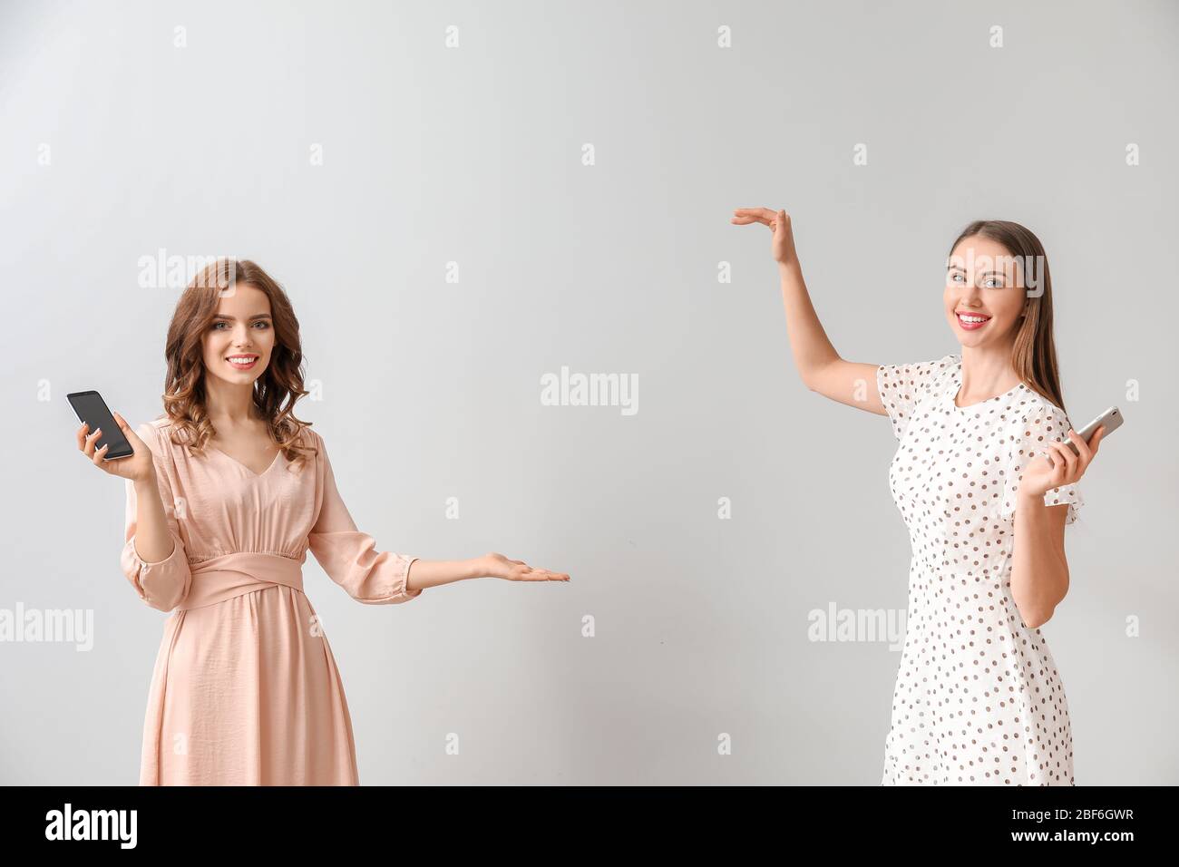 Young women with mobile phones on light background Stock Photo - Alamy
