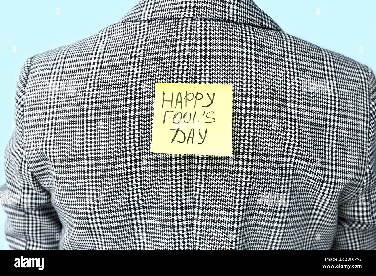 Sticky note with text HAPPY FOOL'S DAY on back of woman against color ...