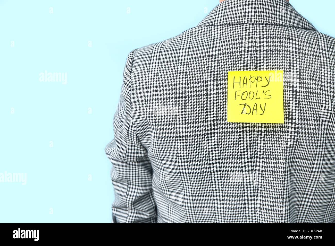 Sticky note with text HAPPY FOOL'S DAY on back of woman against color ...