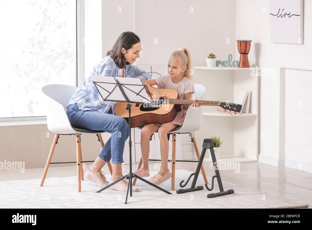 Private music teacher giving guitar lessons to little girl at home ...