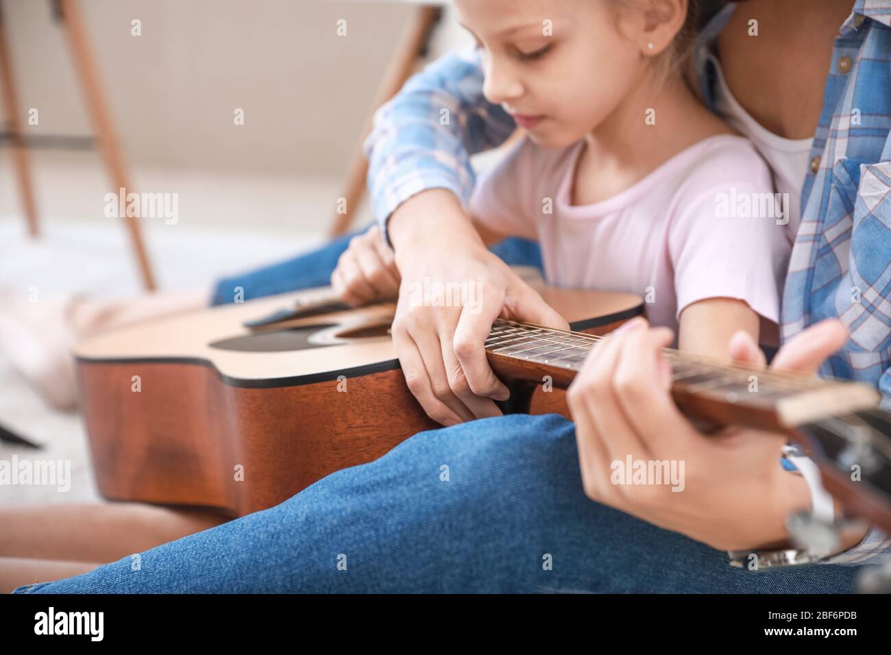 Private music teacher giving guitar lessons to little girl at home ...