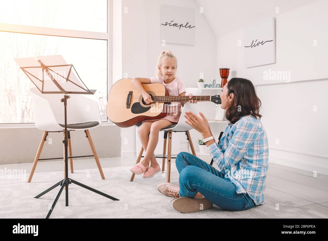 Private music teacher giving guitar lessons to little girl at home ...