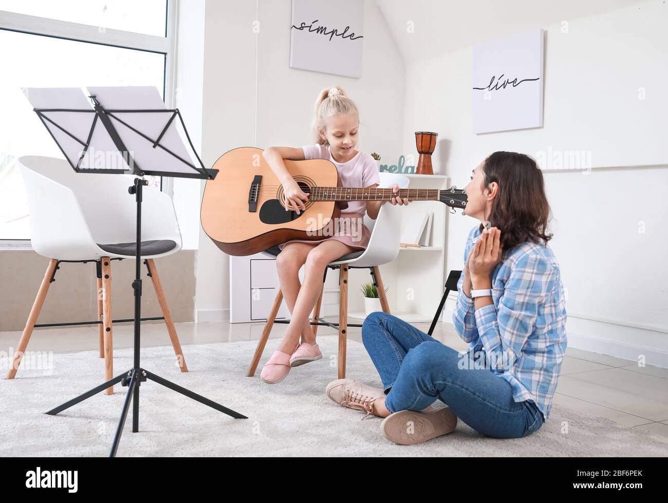 Private music teacher giving guitar lessons to little girl at home ...