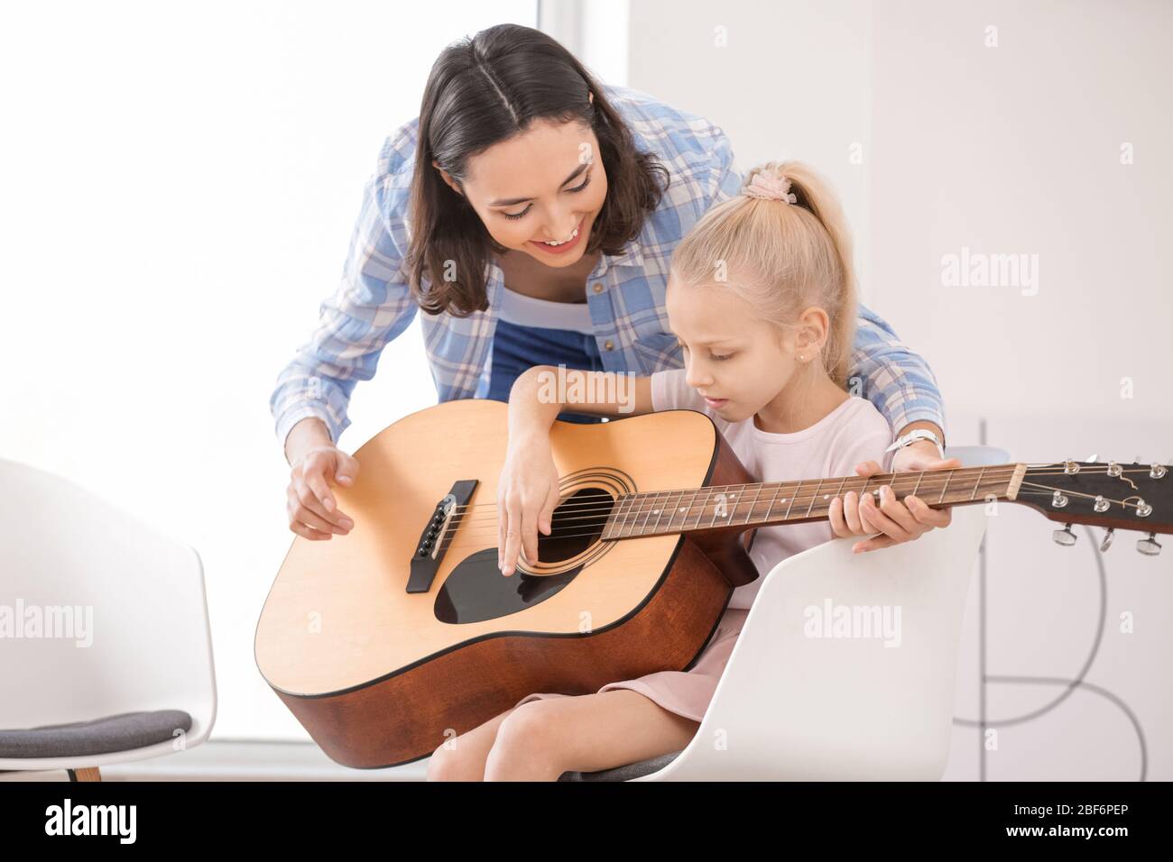 Private music teacher giving guitar lessons to little girl at home ...