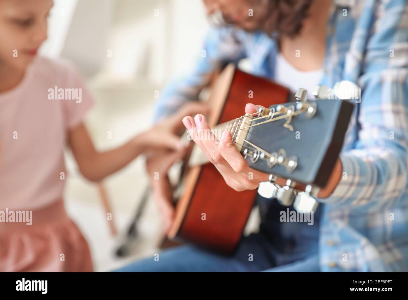 Private music teacher giving guitar lessons to little girl at home ...
