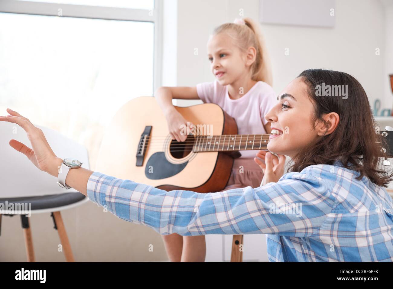 Private music teacher giving guitar lessons to little girl at home ...