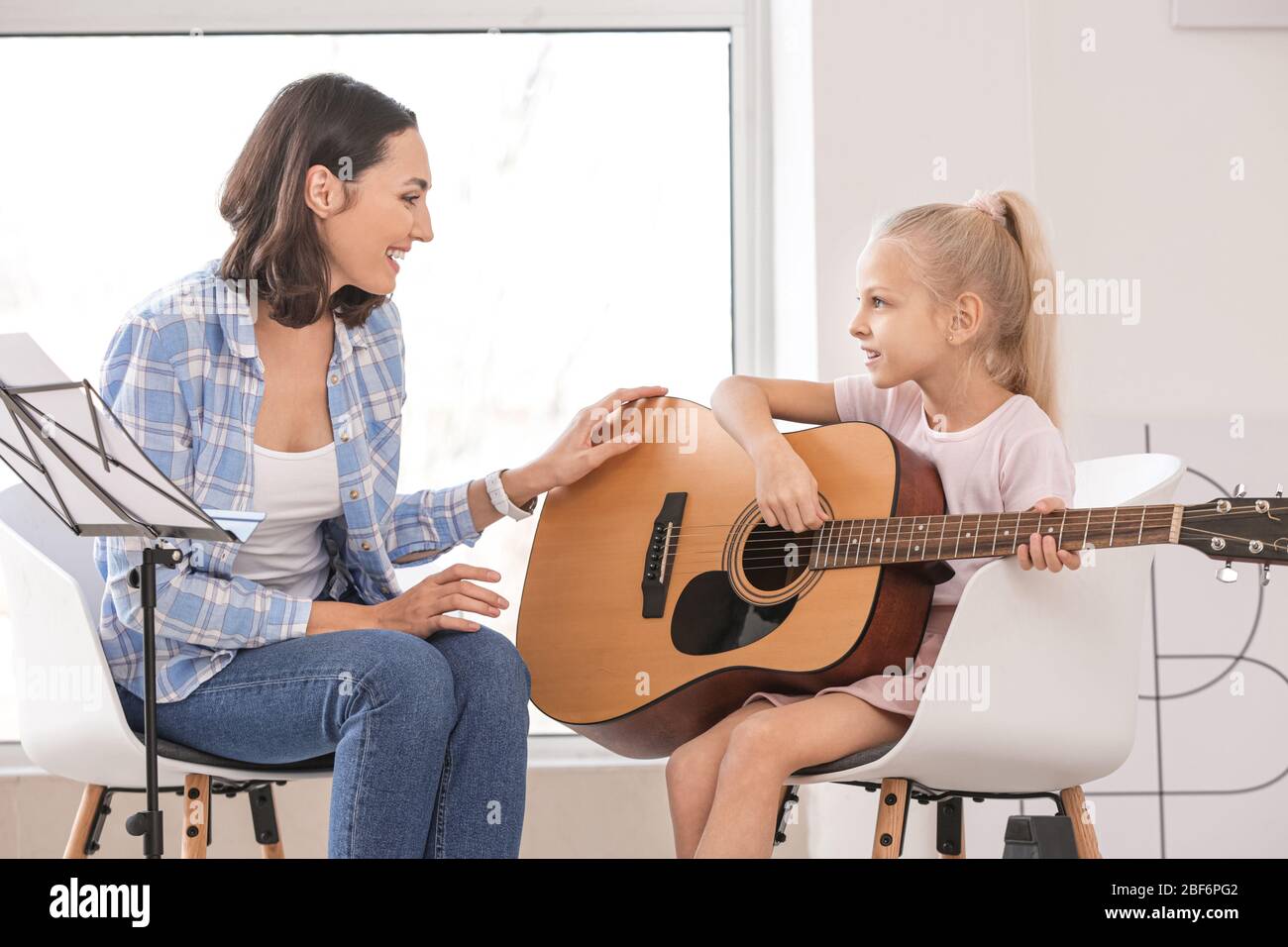 Private music teacher giving guitar lessons to little girl at home ...