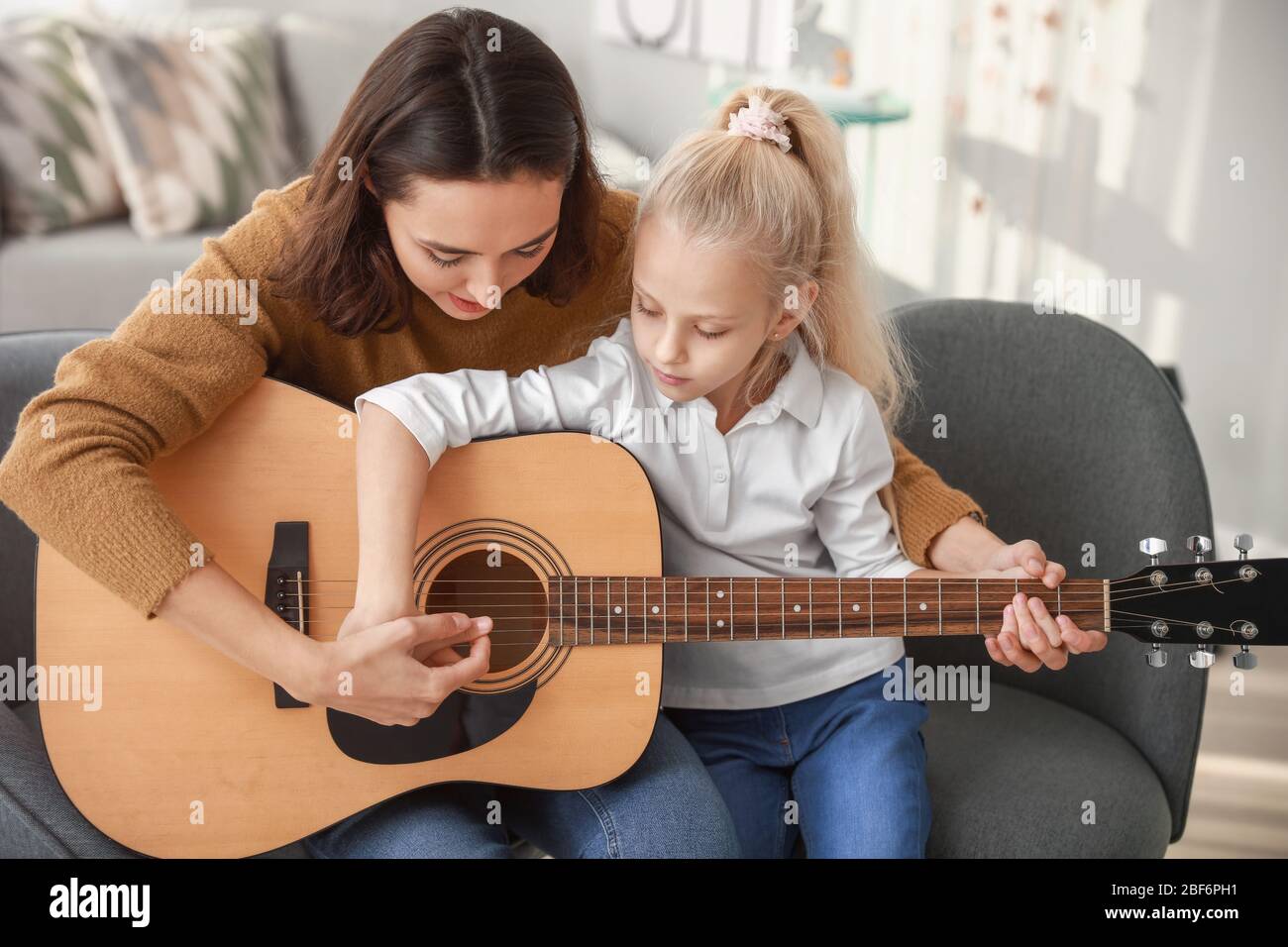 Private music teacher giving guitar lessons to little girl at home ...