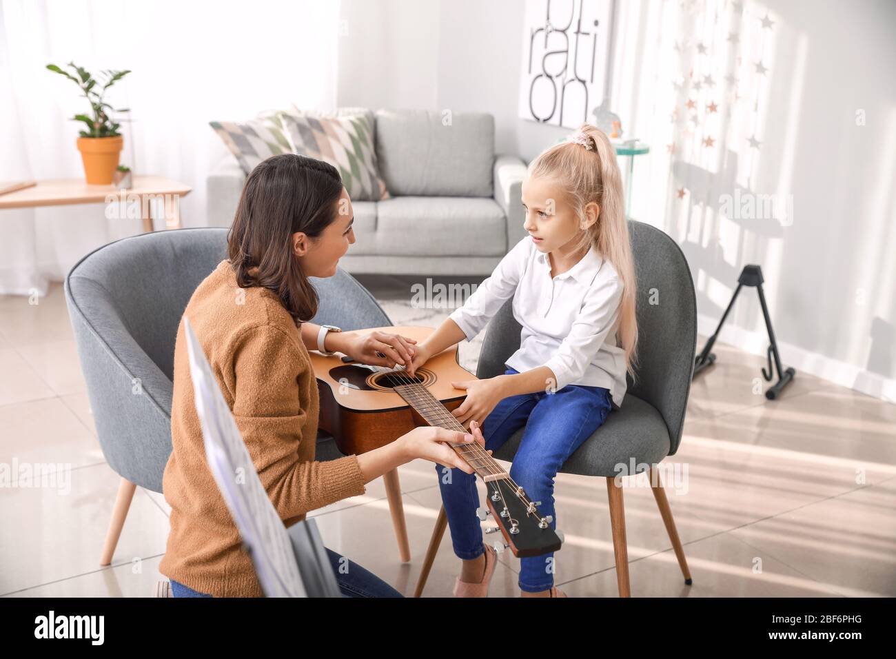 Private music teacher giving guitar lessons to little girl at home ...