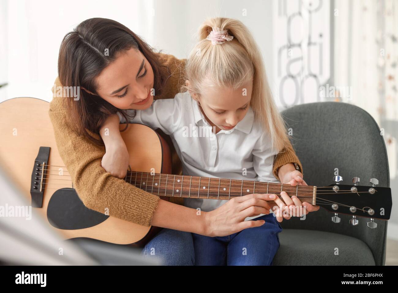 Private music teacher giving guitar lessons to little girl at home ...