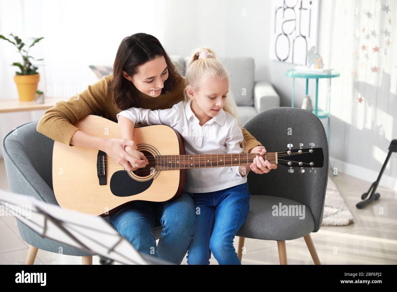 Private music teacher giving guitar lessons to little girl at home ...