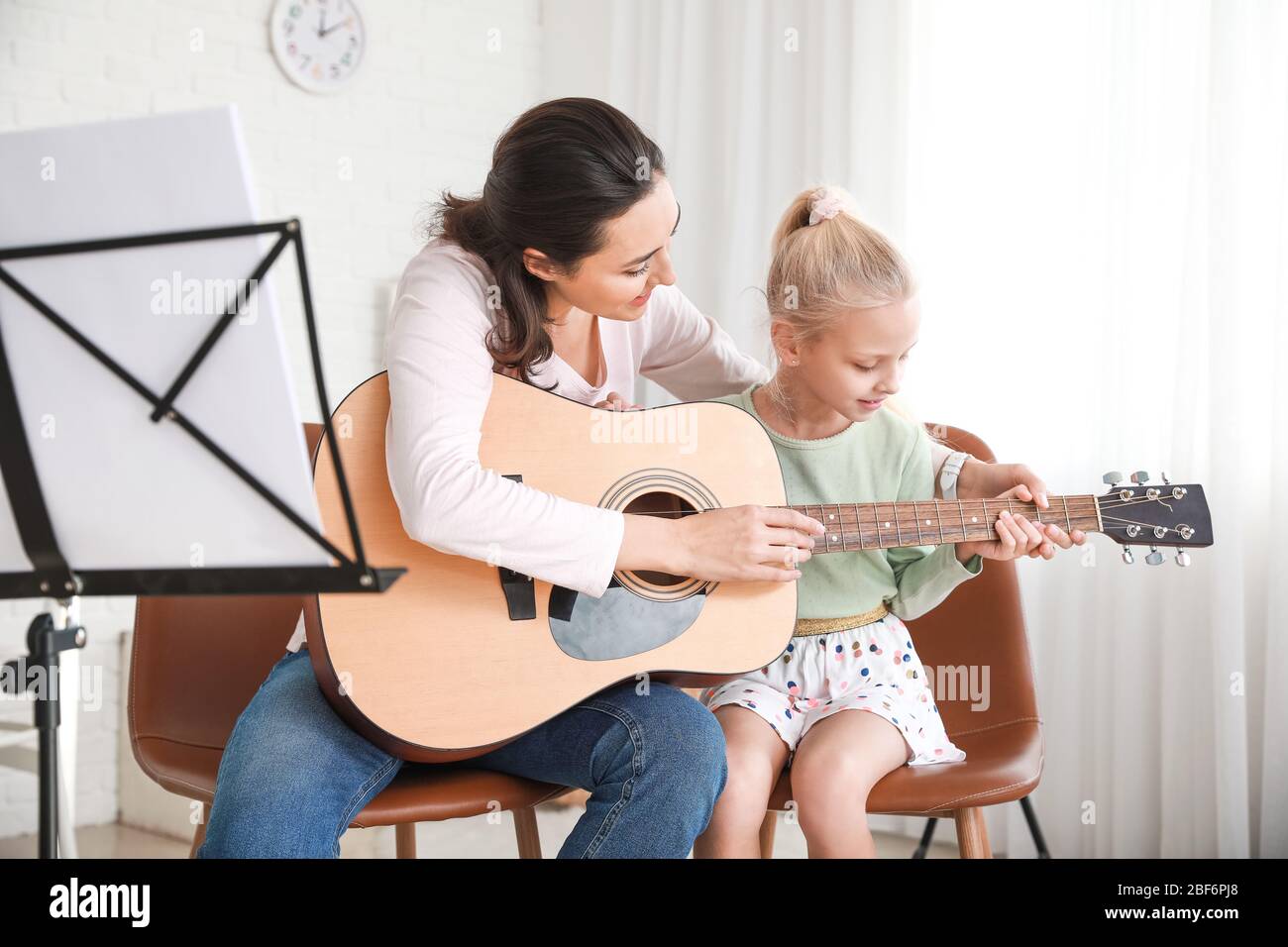 Private music teacher giving guitar lessons to little girl at home ...