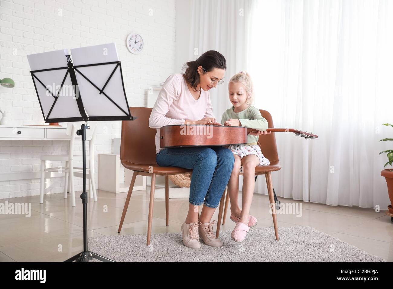 Private music teacher giving guitar lessons to little girl at home ...