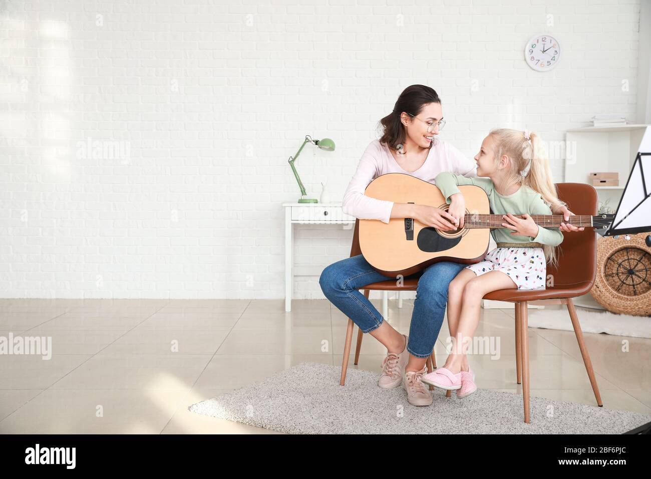 Private music teacher giving guitar lessons to little girl at home ...