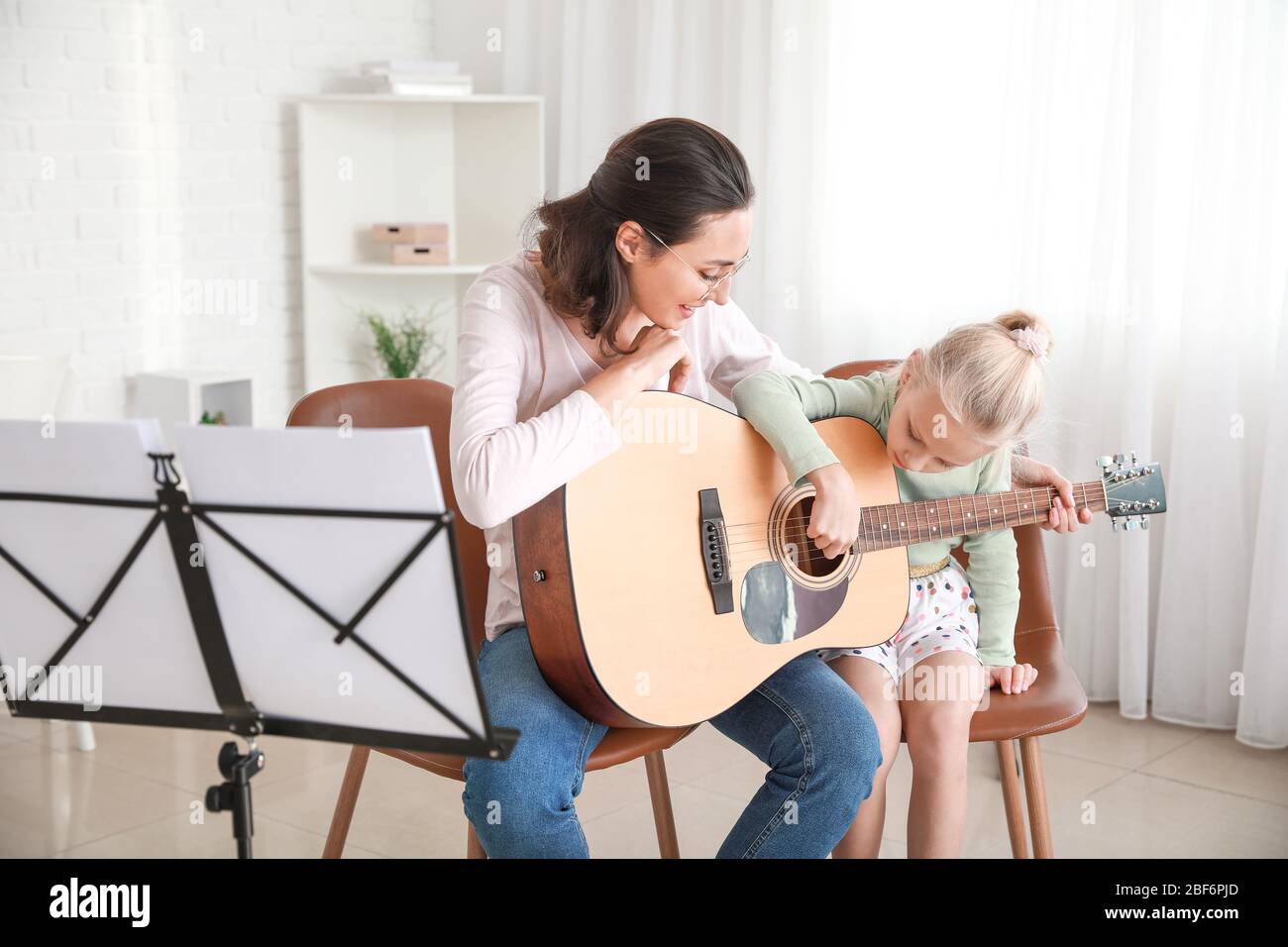 Private music teacher giving guitar lessons to little girl at home ...