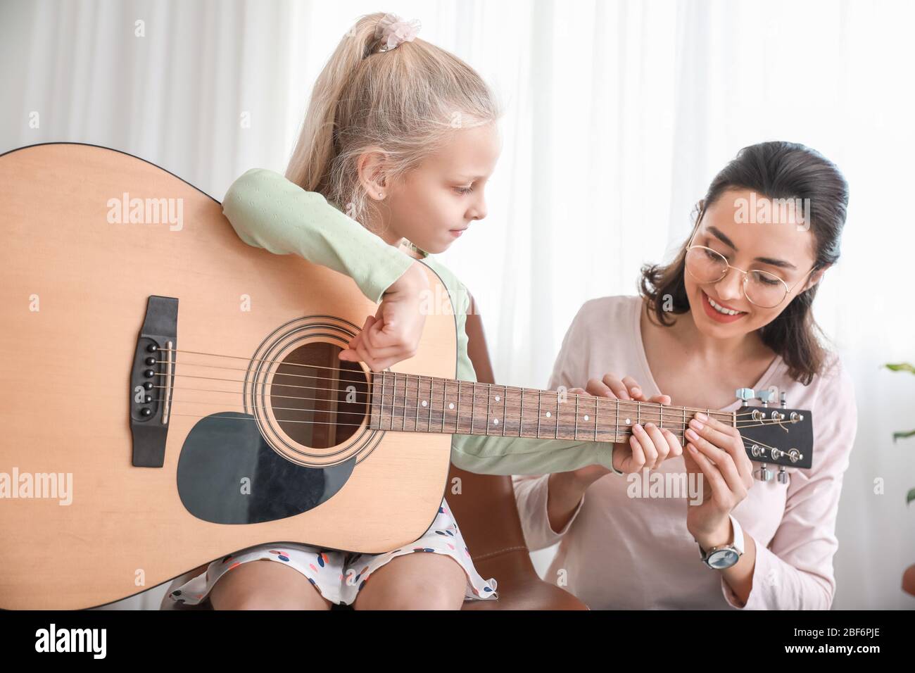 Private music teacher giving guitar lessons to little girl at home ...