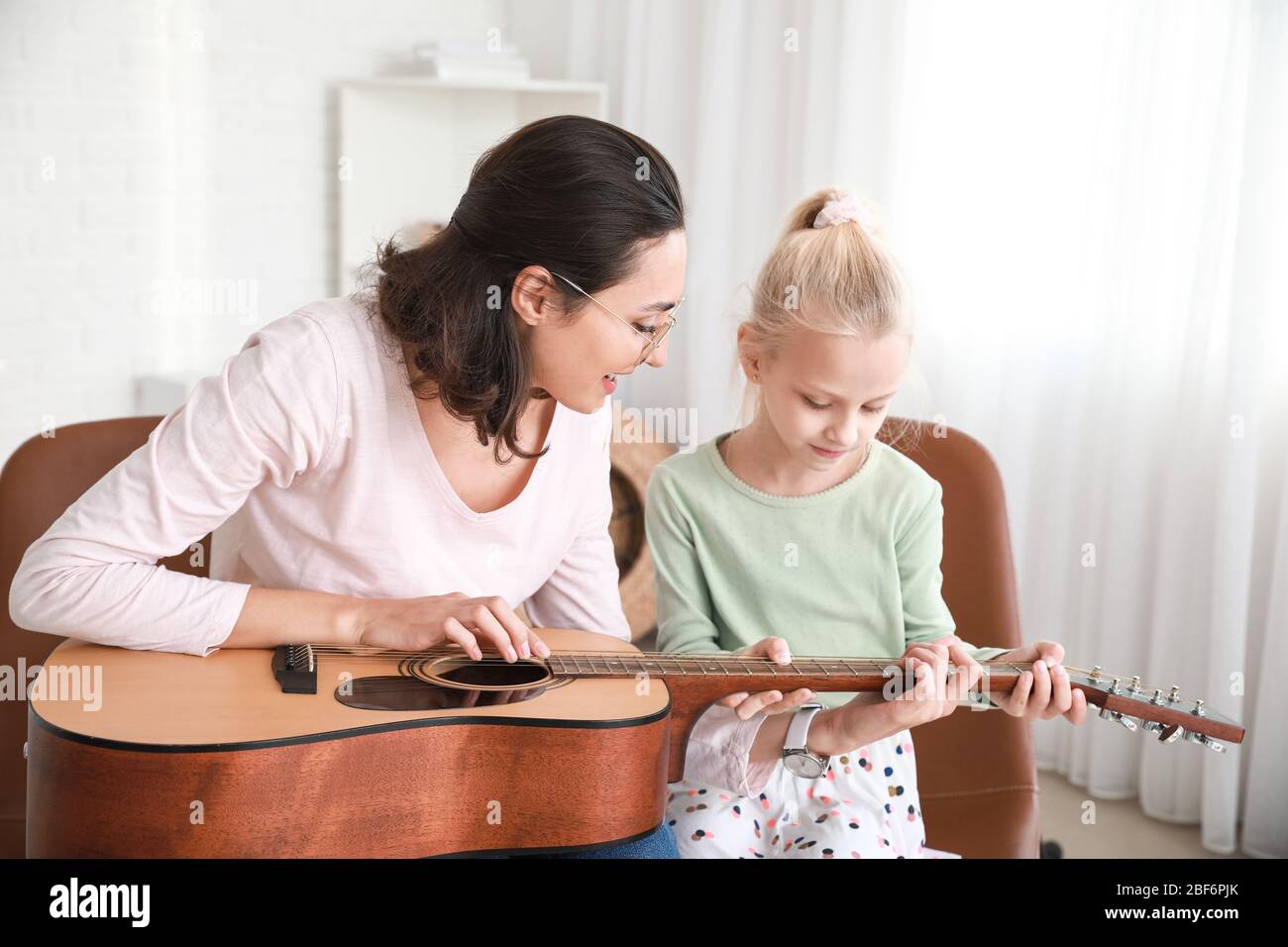 Private music teacher giving guitar lessons to little girl at home ...