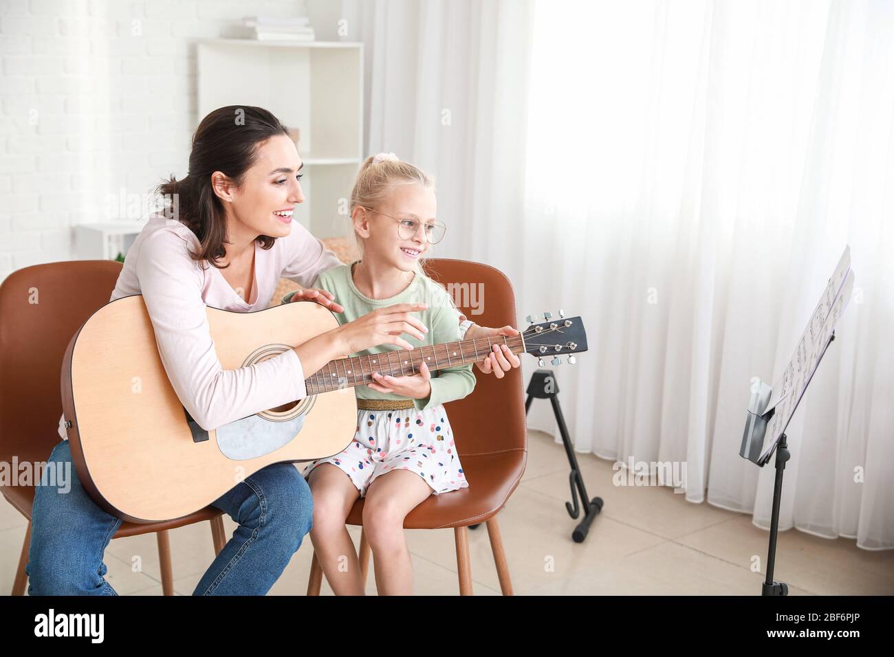 Private music teacher giving guitar lessons to little girl at home ...