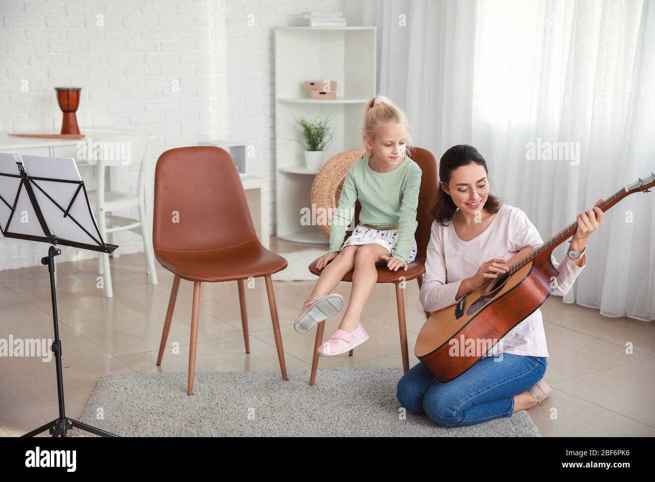 Private music teacher giving guitar lessons to little girl at home ...