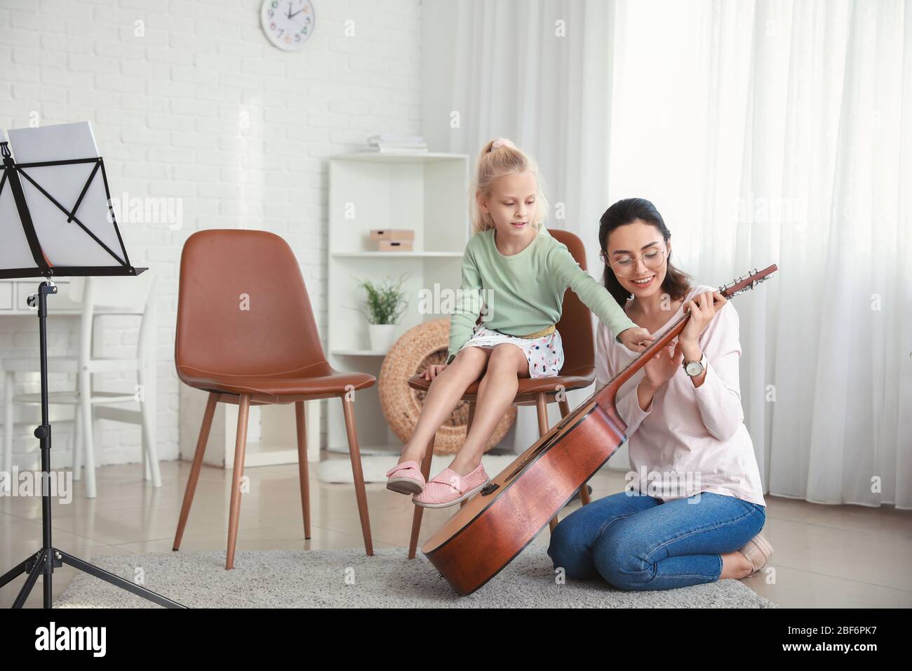 Private music teacher giving guitar lessons to little girl at home ...