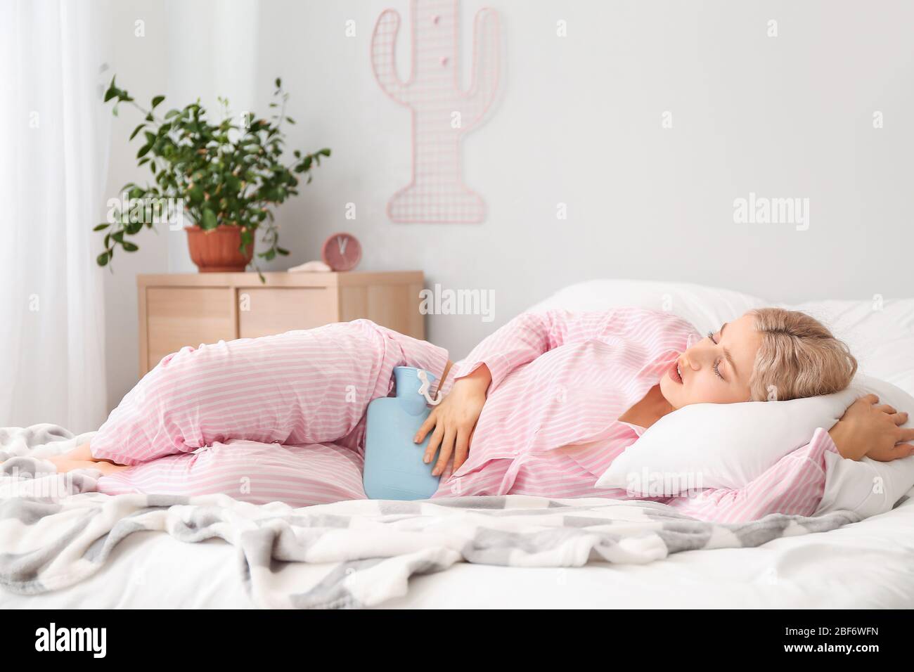 Young woman suffering from menstrual cramps in bedroom Stock Photo - Alamy