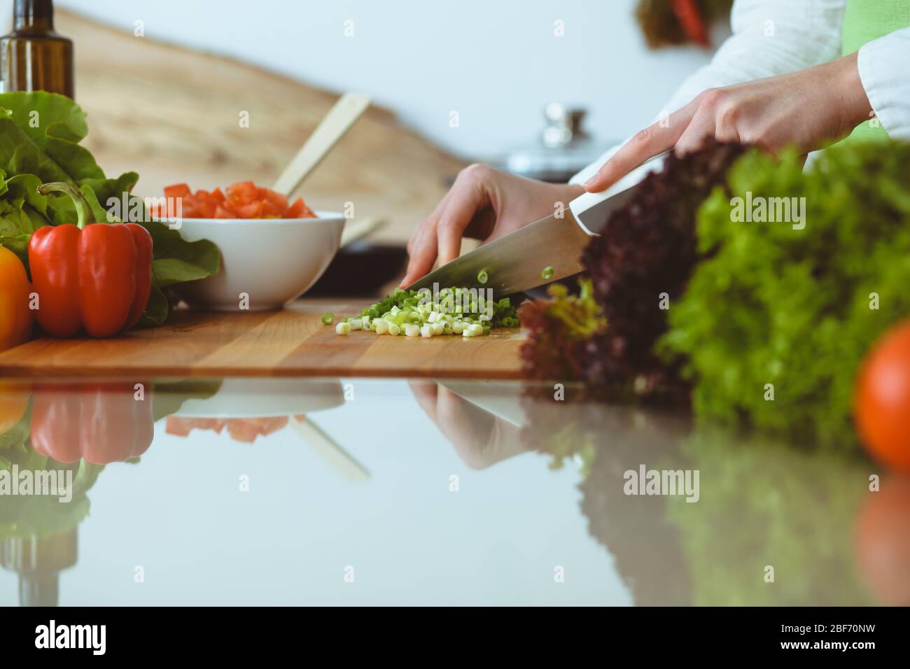 Unknown human hands cooking in kitchen. Woman slicing green onion ...
