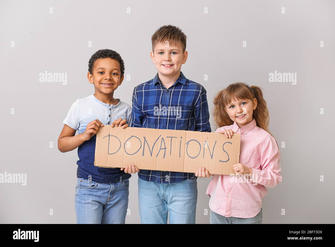 Little children holding cardboard with text DONATIONS on grey ...
