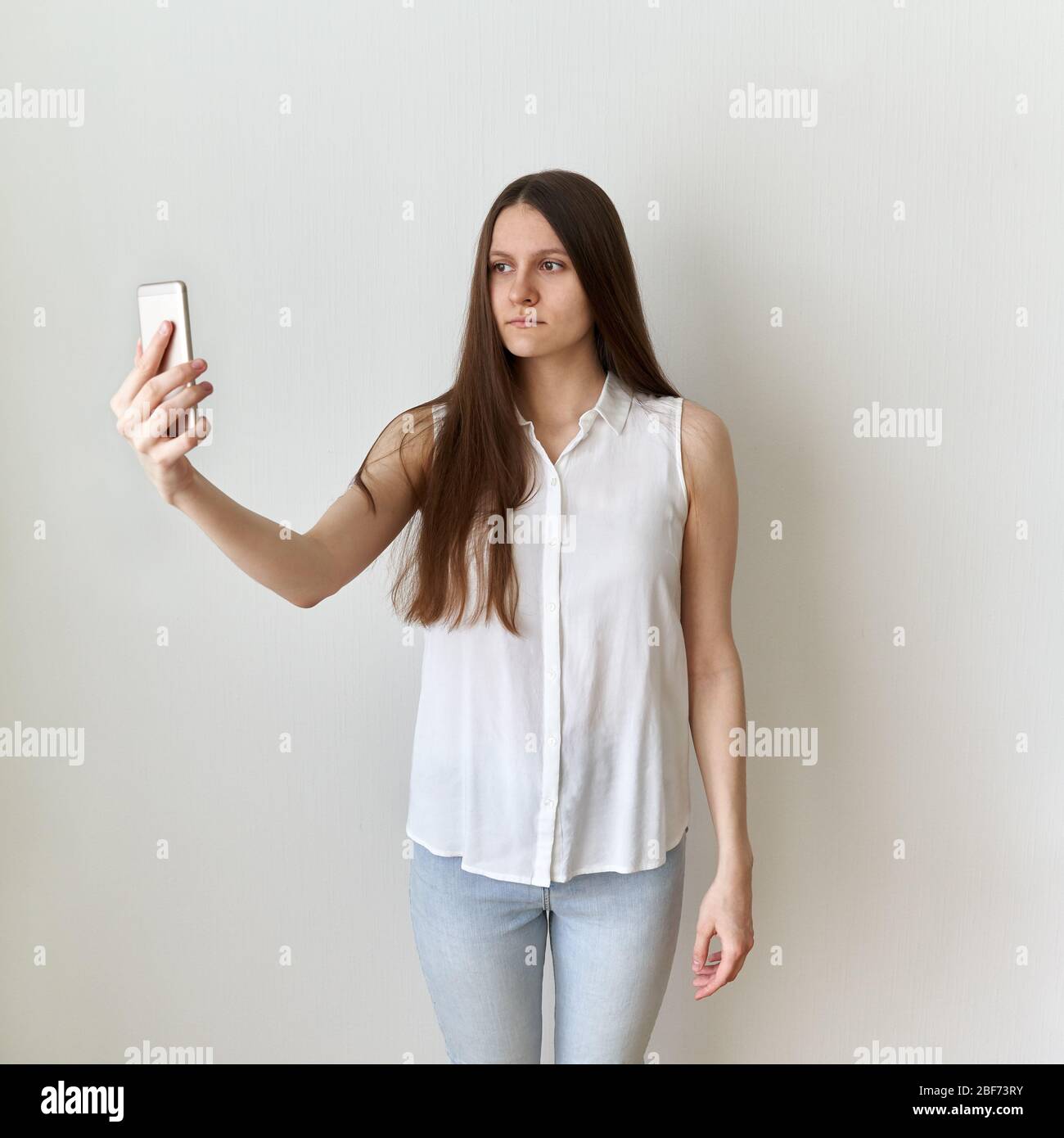 Calm, emotionless woman takes selfie on cell phone. Serious ...