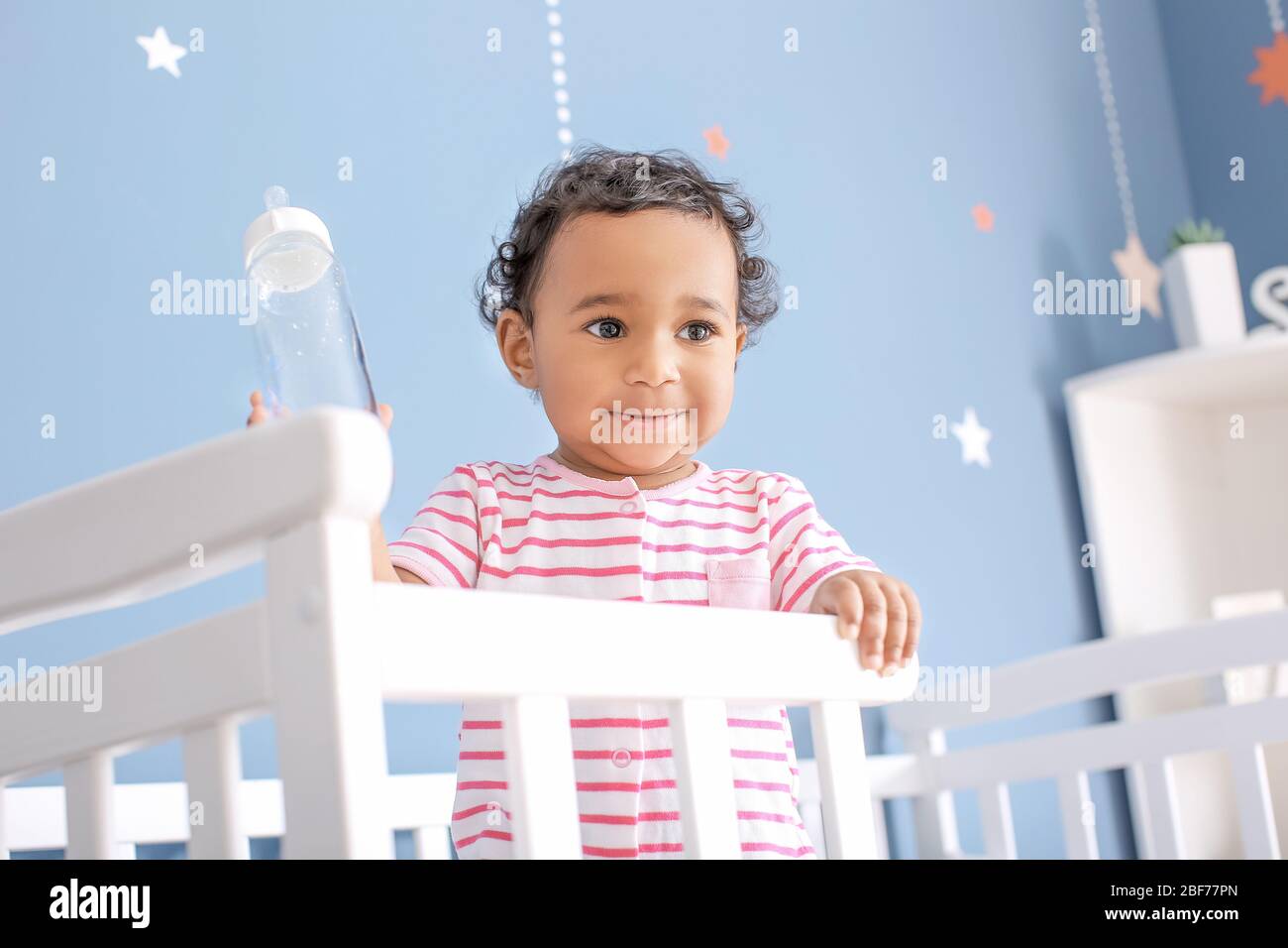 Cute African-American baby with bottle of water in crib Stock Photo - Alamy