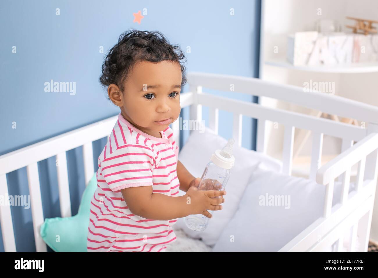 Cute African-American baby with bottle of water in crib Stock Photo - Alamy