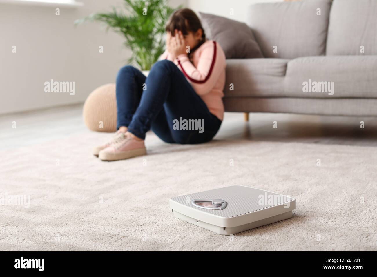 Sad overweight girl with measuring scales at home Stock Photo - Alamy