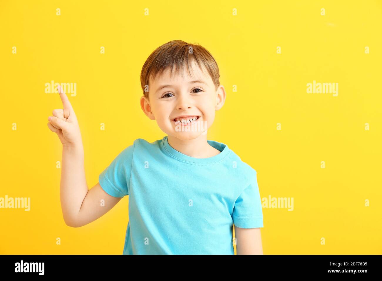 Happy smiling little boy pointing at something on color background ...
